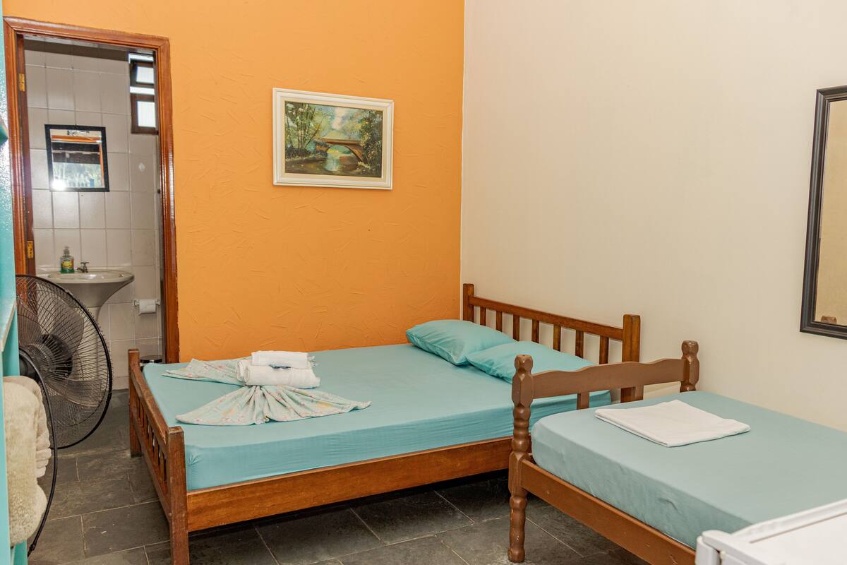 Quarto com duas camas de madeira, uma pia pequena e um ventilador.