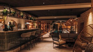 Uma área de bar com balcão curvo, cadeiras de vime e luminárias de vime pendentes.