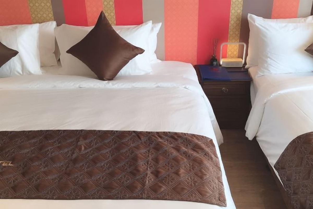 Quarto de hotel com duas camas, uma mesa de cabeceira e uma mesinha de apoio.