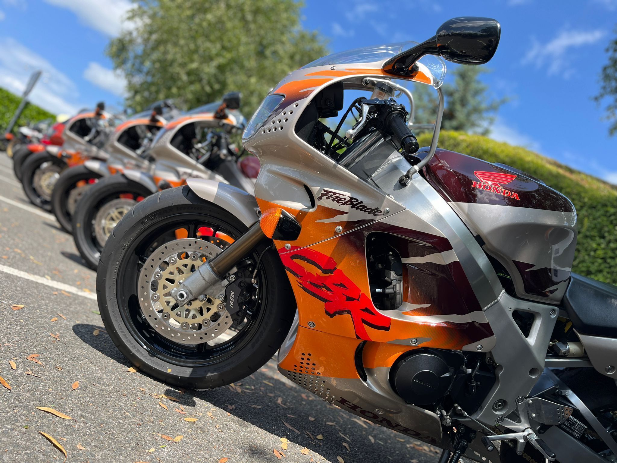 Uma motocicleta com a marcação visível "Fireblade" e "Honda", estacionada em uma fileira na estrada, com árvores ao fundo.