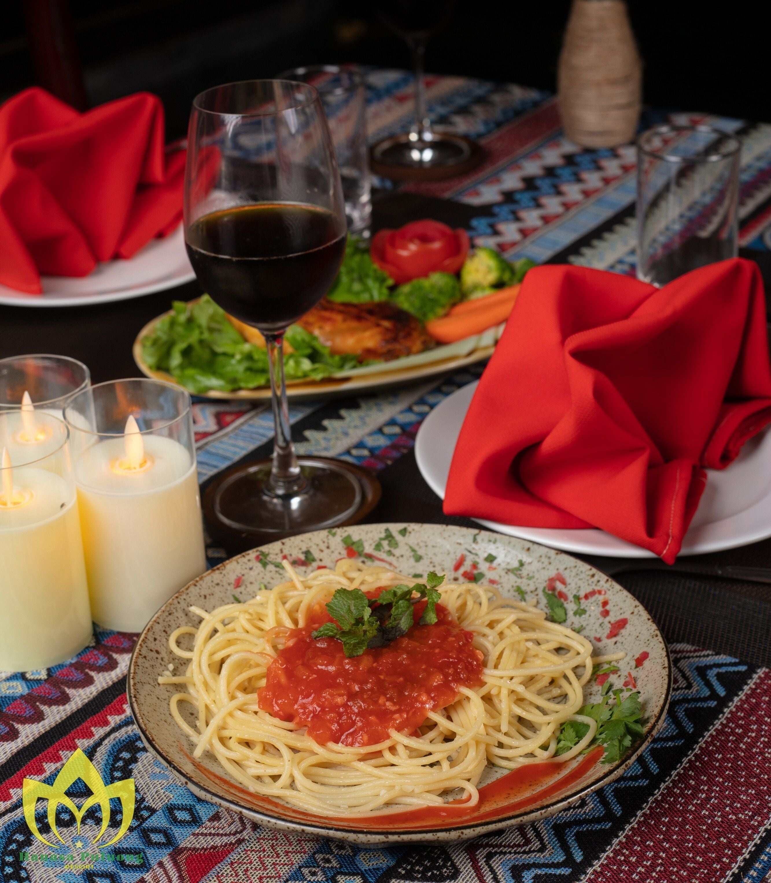 Uma mesa posta com espaguete, um copo de vinho tinto e velas.
