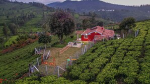 Um edifício vermelho com telhado inclinado, cercado por uma área de recreação com gramado, estruturas para escalar e uma árvore.