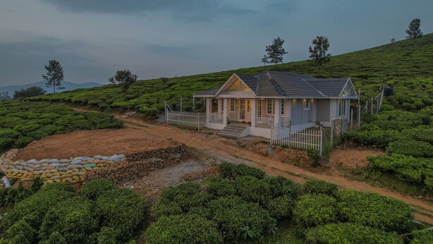 Uma casa com telhado inclinado, cercada por vegetação exuberante e uma paisagem montanhosa.