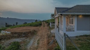 Uma casa com calçada de pedra que leva a um portão, cercada por um muro de pedra e vegetação exuberante.