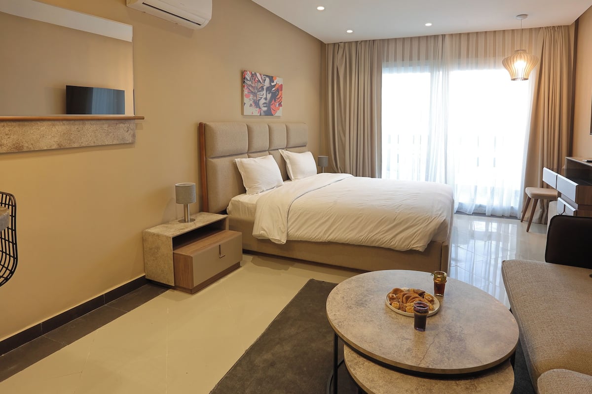 Quarto de hotel moderno com uma cama grande, uma escrivaninha, um sofá e uma mesa de jantar com comida.
