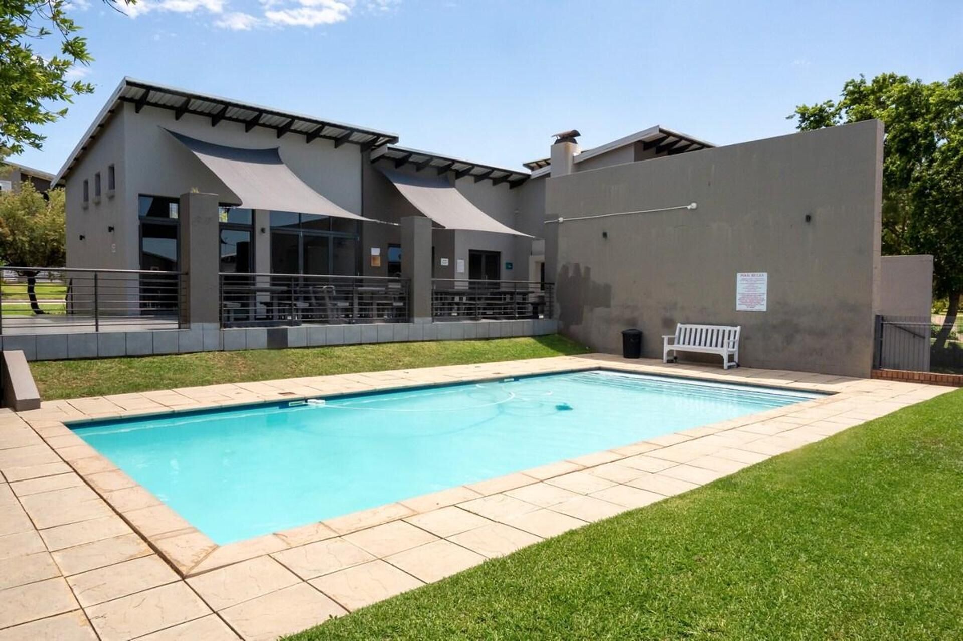 Um edifício moderno com piscina, área gramada e um banco.