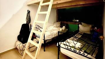 Um quarto em dormitório com beliches, escada, cadeira e uma pequena mesa.