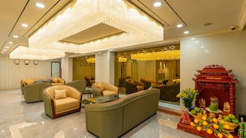 Um lobby moderno com sofás, uma mesa de centro de vidro, um altar decorativo e um grande candelabro.