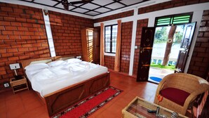 Quarto com uma cama grande, uma cadeira de vime, uma mesa pequena e vista para o exterior através de uma porta.