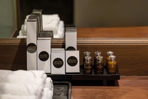Quarto de hotel com artigos de higiene pessoal bem organizados e uma mesa de cabeceira de madeira.