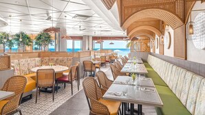 Restaurante com vista para o oceano, com móveis de vime, assentos acolchoados verdes e design moderno no teto.