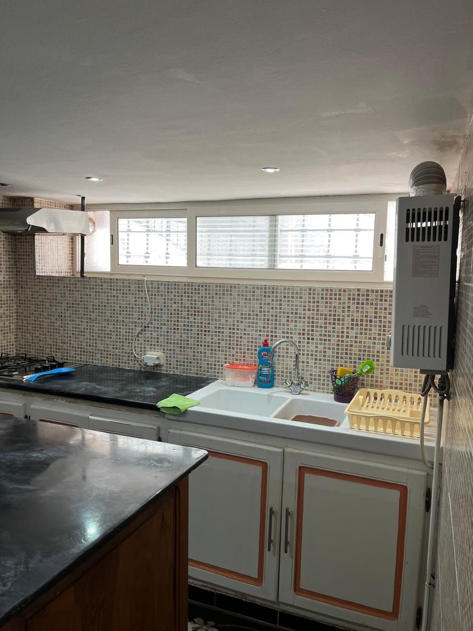 Uma cozinha com bancada preta, armários brancos, uma janela sobre a pia e painel de azulejos.