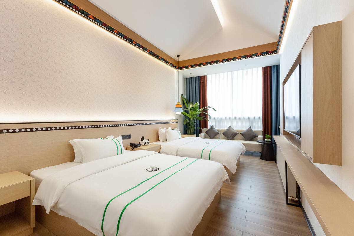 Quarto de hotel com duas camas, um espelho grande, uma televisão e uma janela com cortinas.