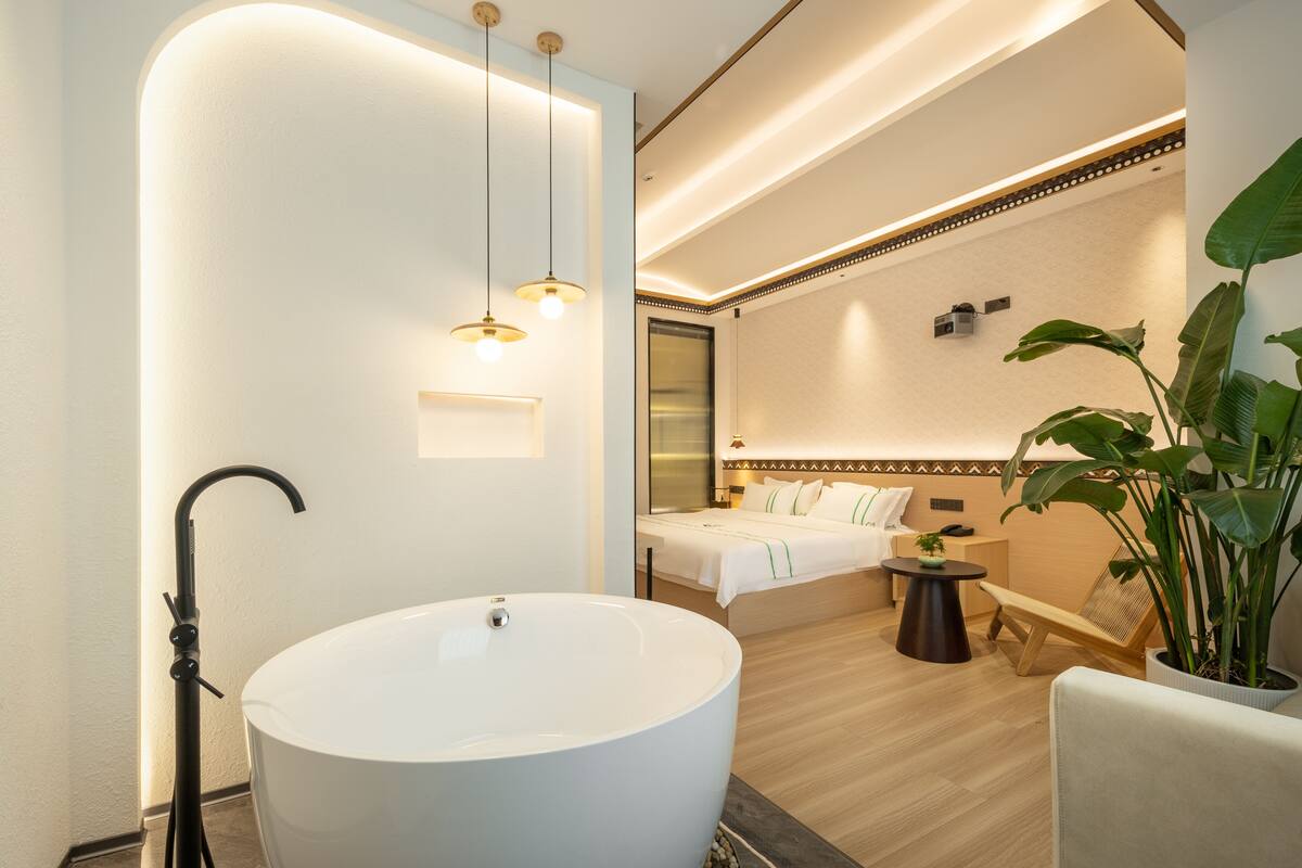 Um banheiro moderno com uma banheira independente, um lavatório e uma cama no quarto adjacente.
