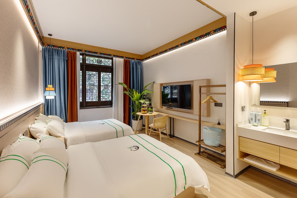 Quarto de hotel com duas camas, televisão, secretária e banheiro.