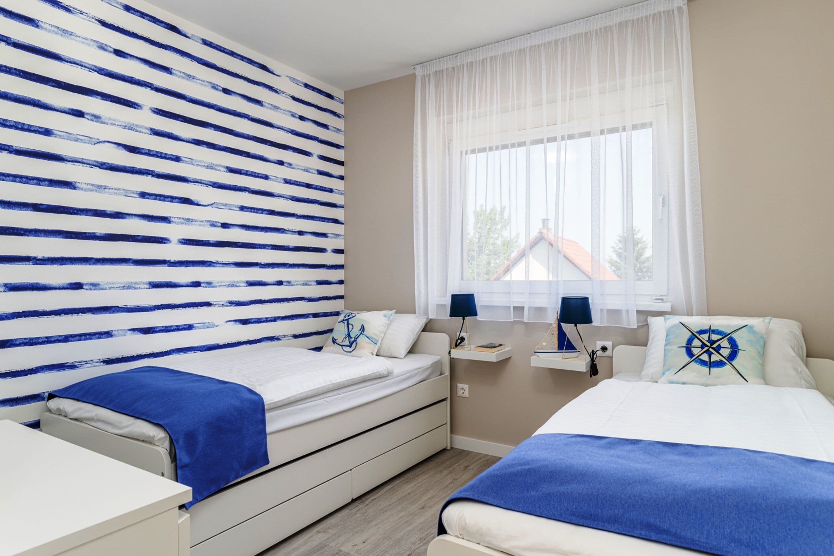 Quarto com cama, mesas de cabeceira, janela com cortinas e parede com padrão listrado.