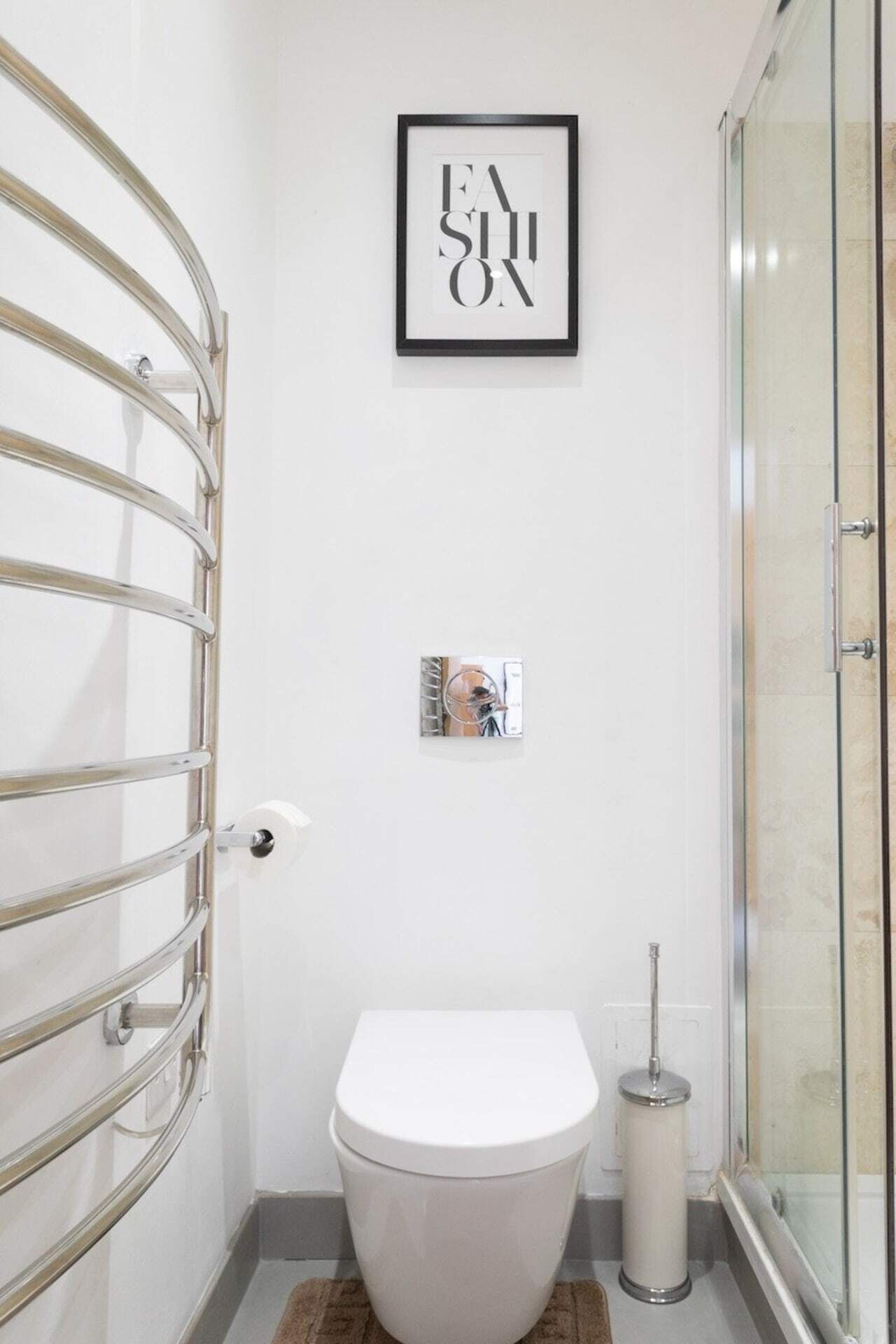 Um banheiro com vaso sanitário branco, um quadro pendurado na parede e área de chuveiro.