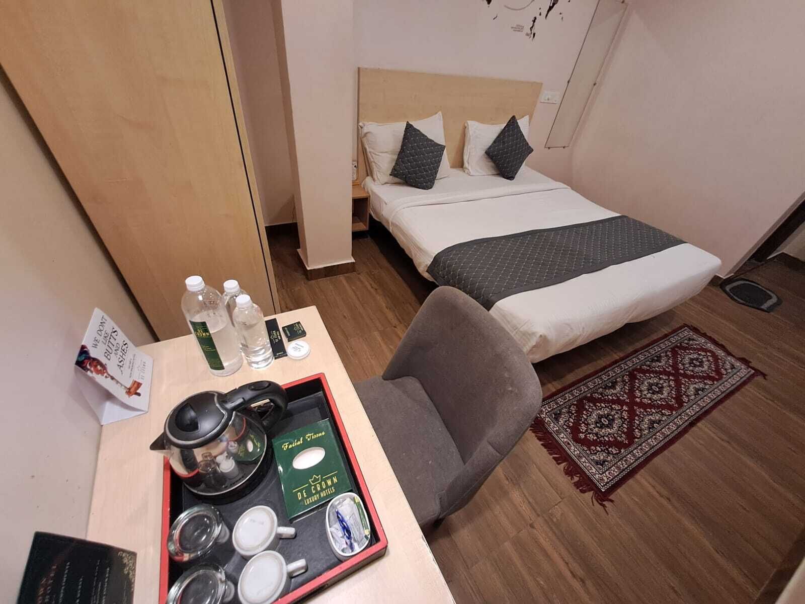 Quarto de hotel com cama, escrivaninha e produtos de higiene pessoal, e uma cadeira.