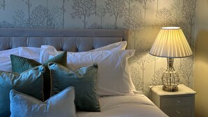 Uma cama bem arrumada com almofadas brancas e verdes, uma cabeceira cinzenta e uma mesa de cabeceira com um abajur.