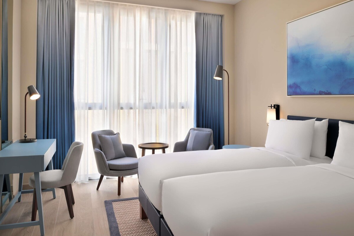 Quarto de hotel com uma cama grande, duas poltronas, uma escrivaninha e uma mesinha.