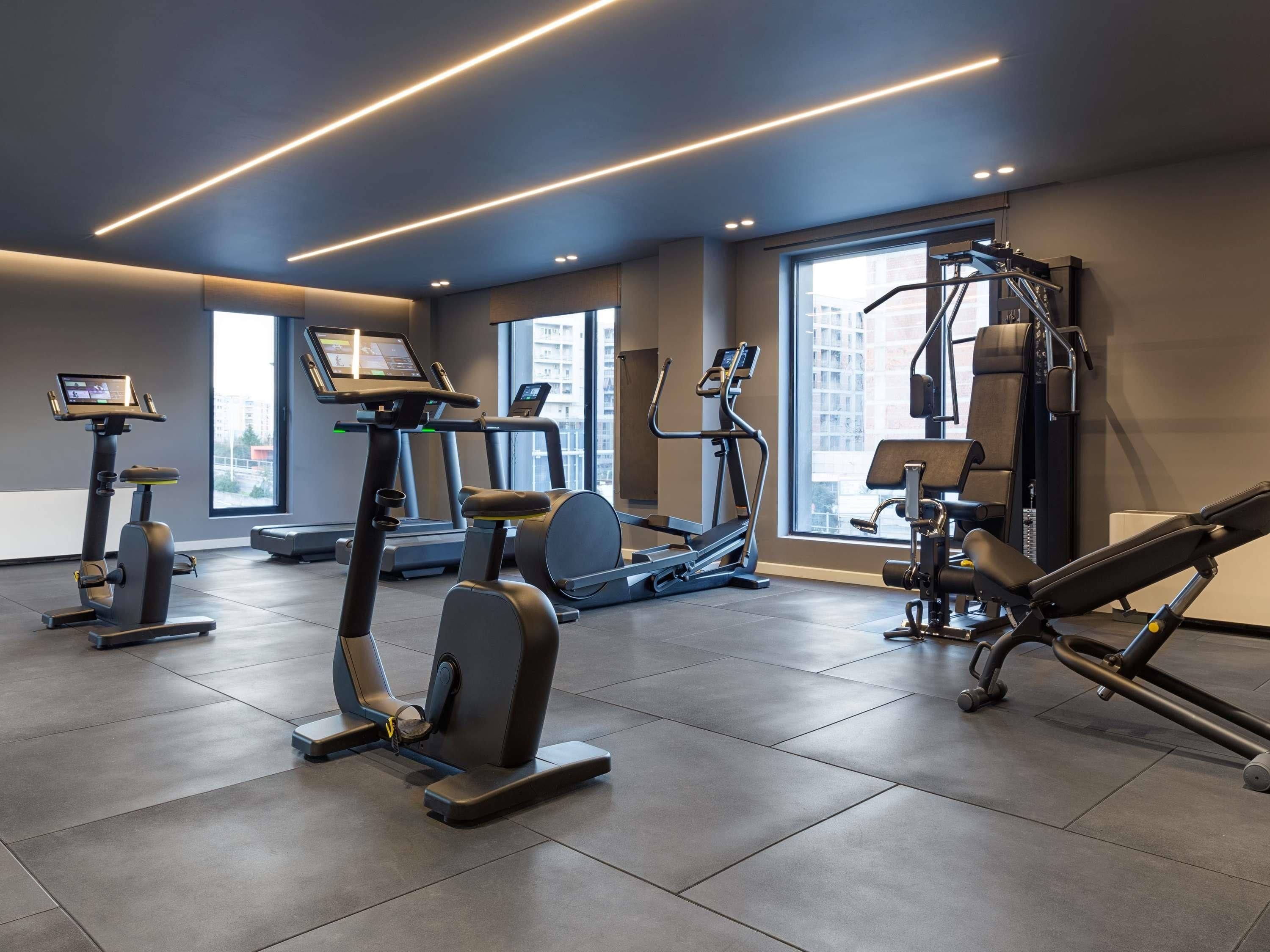 Uma academia moderna com diversos equipamentos de exercício, amplas janelas e um layout espaçoso e arejado.
