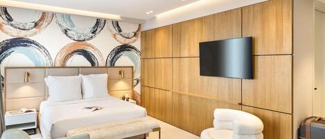 Quarto de hotel moderno com cama, sofá, área de estar, televisão e guarda-roupa.