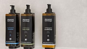 Três frascos de produtos Elemental Herbology: shampoo, hidratante corporal e condicionador.