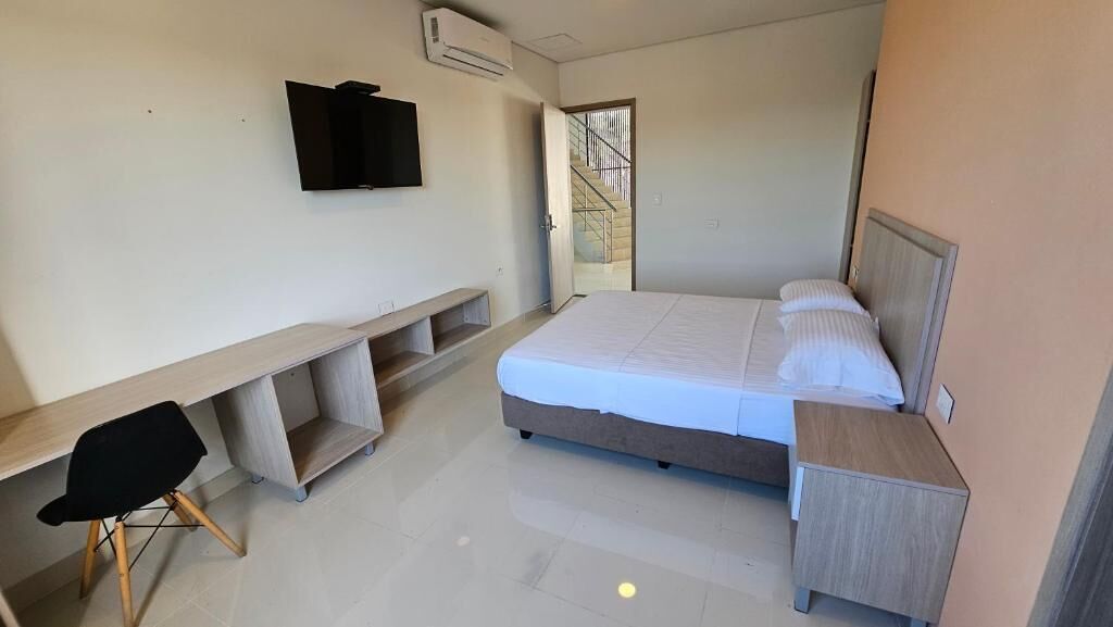 Um quarto com cama, escrivaninha, cadeira, televisão e escada que leva a outro cômodo.