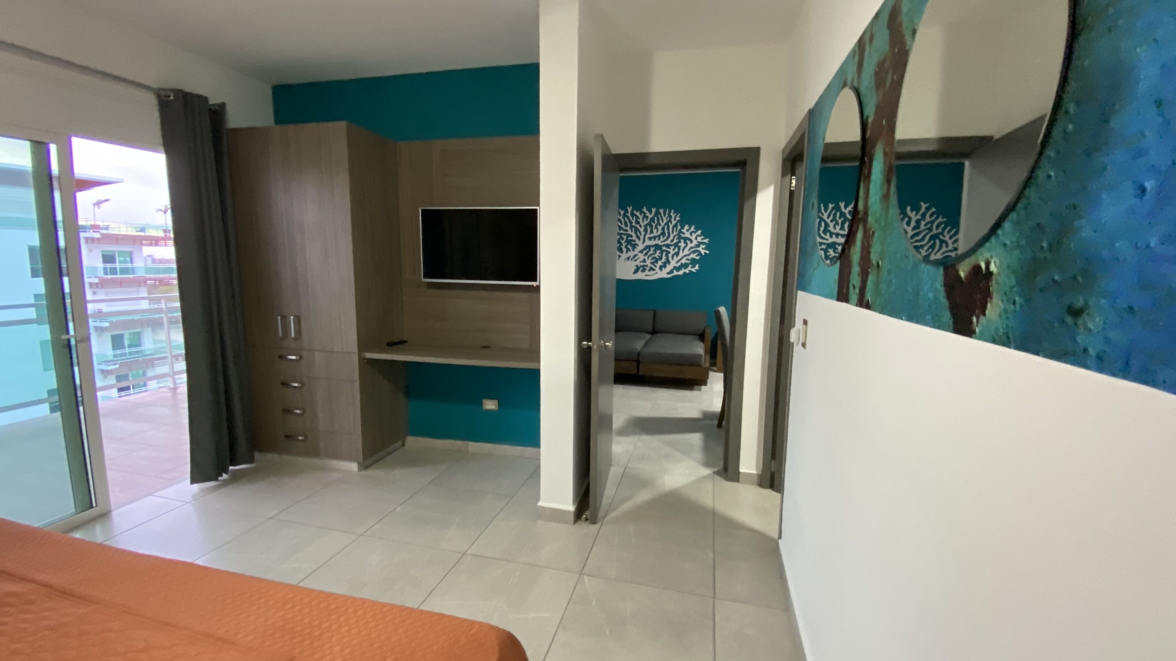Quarto de hotel moderno com uma cama grande, televisão e vista para a varanda externa.