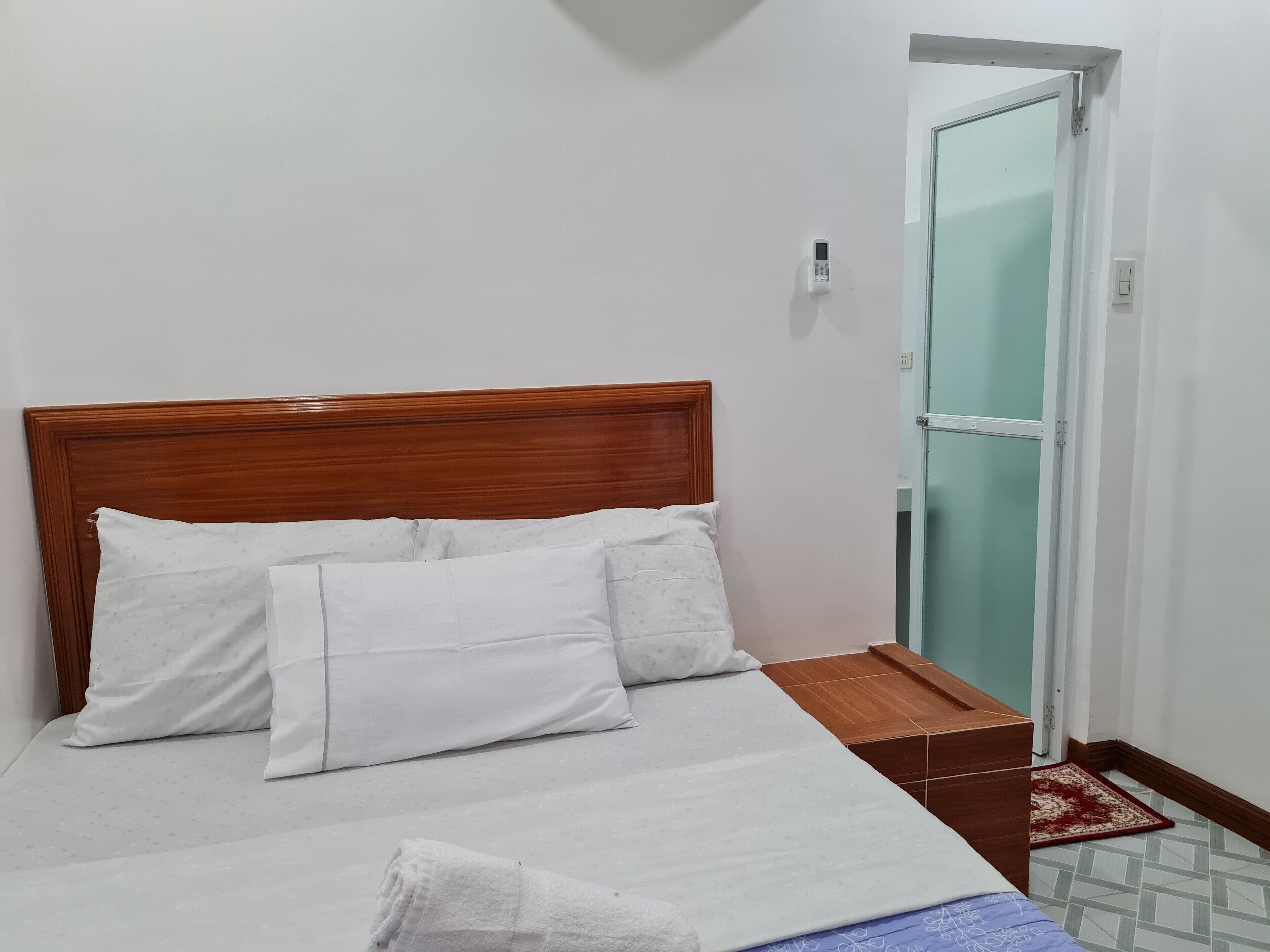 Uma cama bem arrumada com cabeceira de madeira, almofadas brancas e edredom branco.