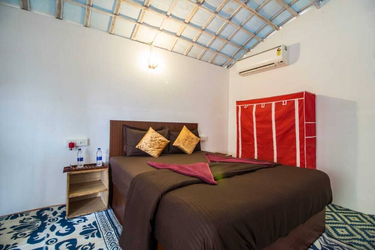 Quarto com uma cama, uma pequena estante de madeira, um guarda-roupa vermelho e um chão estampado.