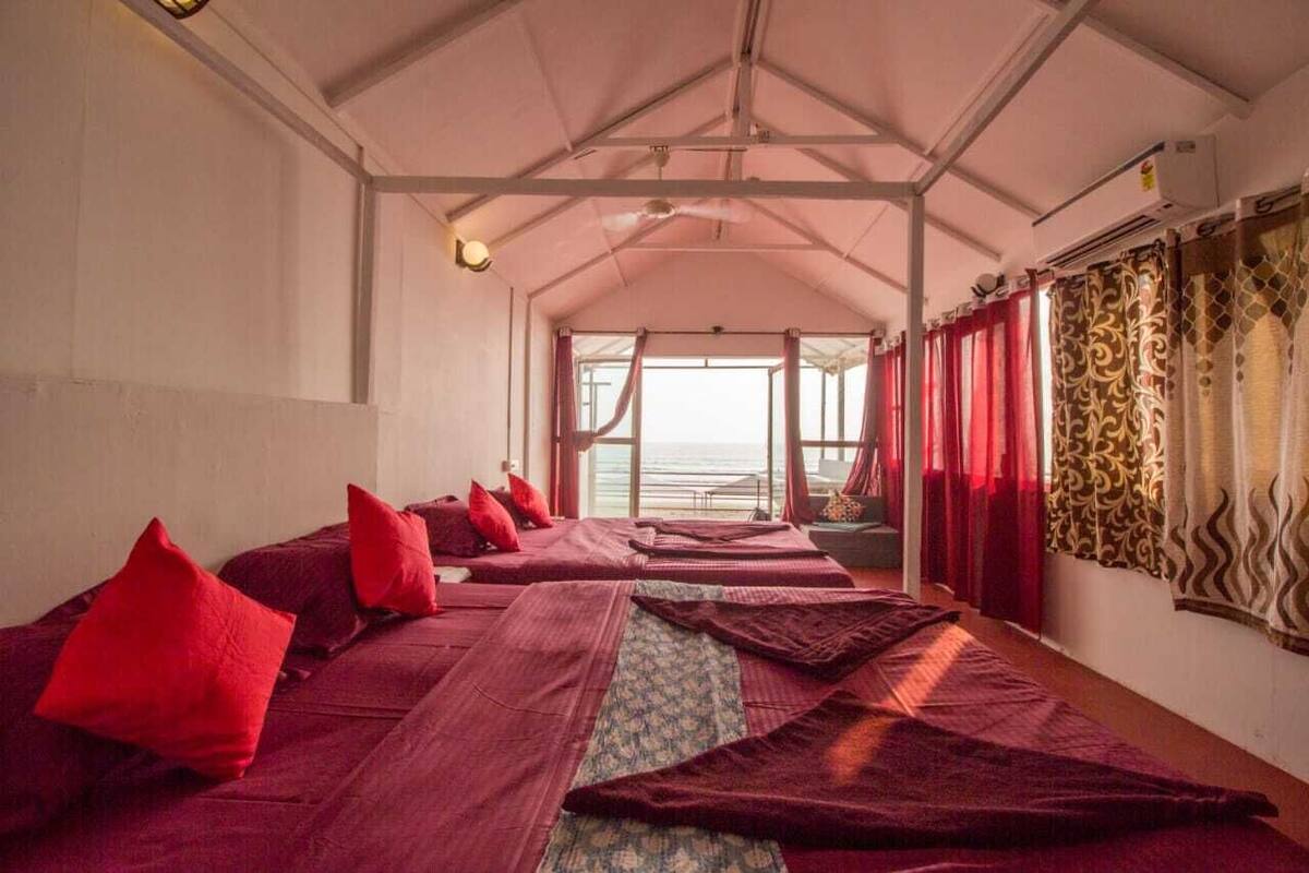 Fileira de camas com roupa de cama vermelha e vista para o mar através de grandes janelas.