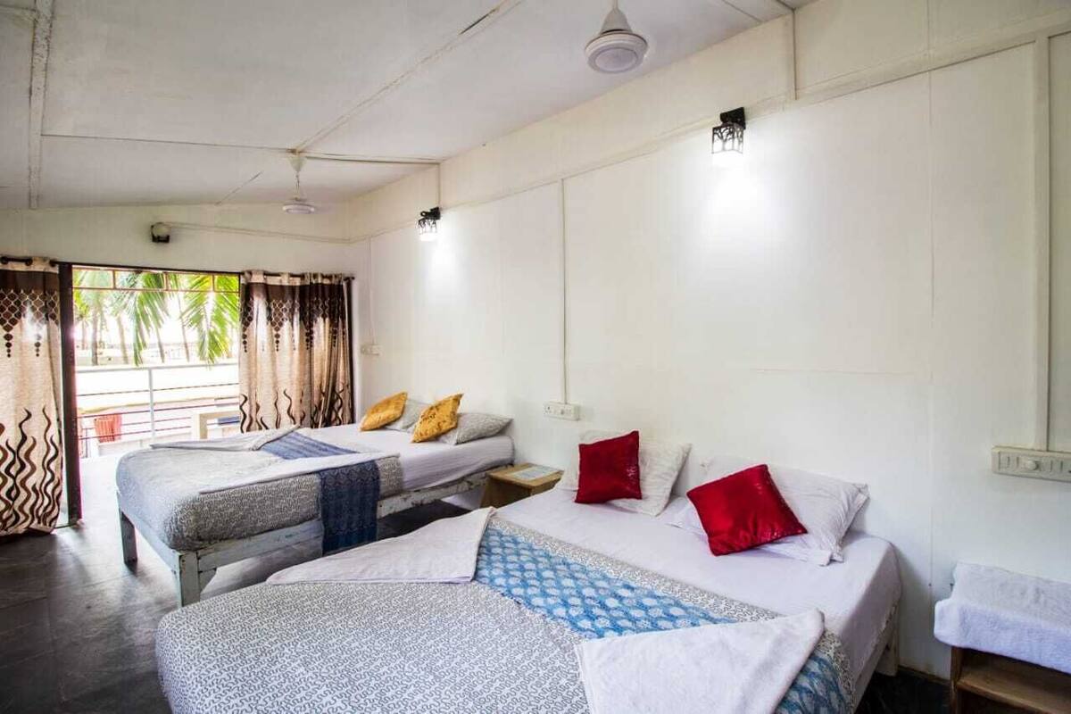 Quarto com duas camas, ventilador de teto e janela com cortinas.