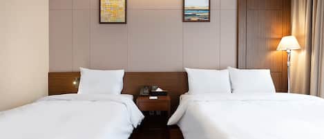 Quarto de hotel com duas camas, uma cabeceira de madeira, mesa de cabeceira com telefone e caixa de lenços, e duas imagens emolduradas na parede.