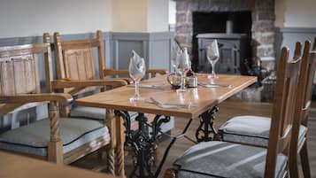 Uma sala de jantar com uma mesa de madeira posta para quatro pessoas, rodeada por cadeiras de madeira com assentos acolchoados.