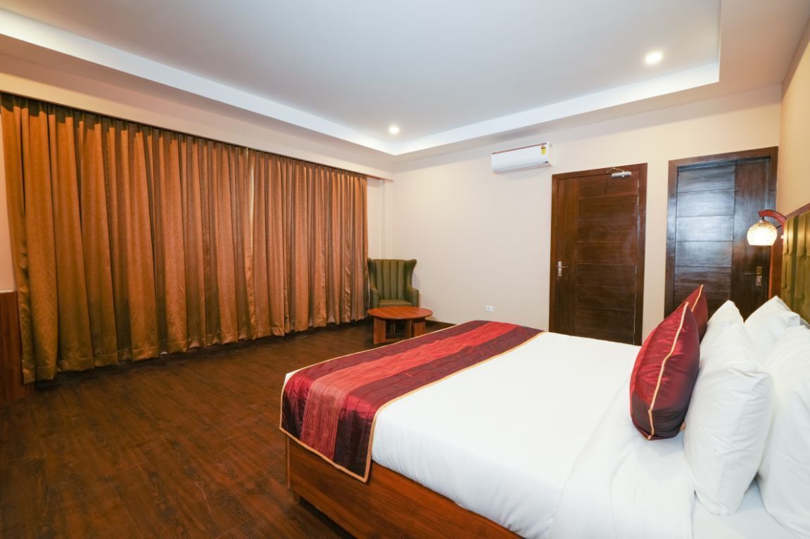 Quarto de hotel com uma cama grande, uma mesinha, uma cadeira e um guarda-roupa.