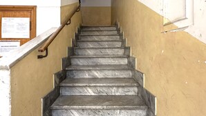 Uma escadaria de mármore com corrimão, que leva a um patamar com um mural de avisos.