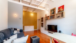 Uma sala de estar moderna com um sofá cinza, piso de madeira, uma mesa pequena e uma televisão.