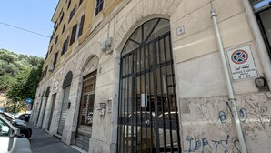 Um edifício de vários andares com fachada amarela, grandes janelas em arco e entrada com portão.