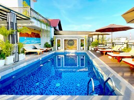 Uma piscina no terraço com espreguiçadeiras e guarda-sóis, cercada por plantas em vasos e um mural.