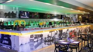 Uma área de bar com um balcão comprido, diversos frascos e uma tela de televisão.
