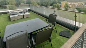 Uma varanda com mesa e cadeiras, uma pequena lareira e vista para os arredores.
