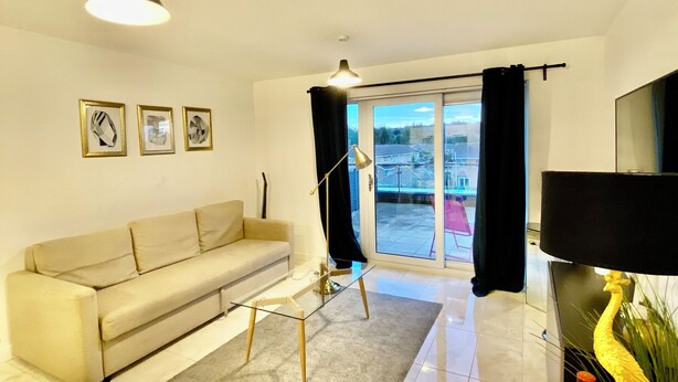 Uma sala de estar moderna com um sofá, uma mesa de centro de vidro e vista para o exterior através de grandes janelas.