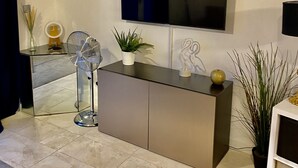 Uma sala de estar moderna com televisão de tela plana na parede, uma mesa de centro de vidro, uma planta em vaso e uma escultura decorativa.