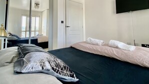 Quarto de hotel com cama, televisão presa na parede, porta e espelho.