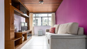 Uma sala de estar moderna com um móvel de entretenimento de madeira, um sofá bege e uma grande janela com cortinas.