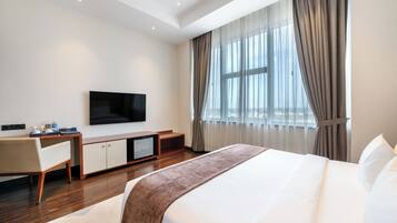 Quarto de hotel com uma cama grande, televisão de tela plana, escrivaninha com cadeira e janela com cortinas.