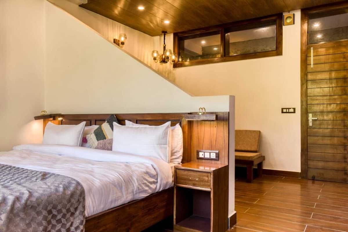 Quarto com cama de madeira, mesa de cabeceira, banqueta e porta de madeira.