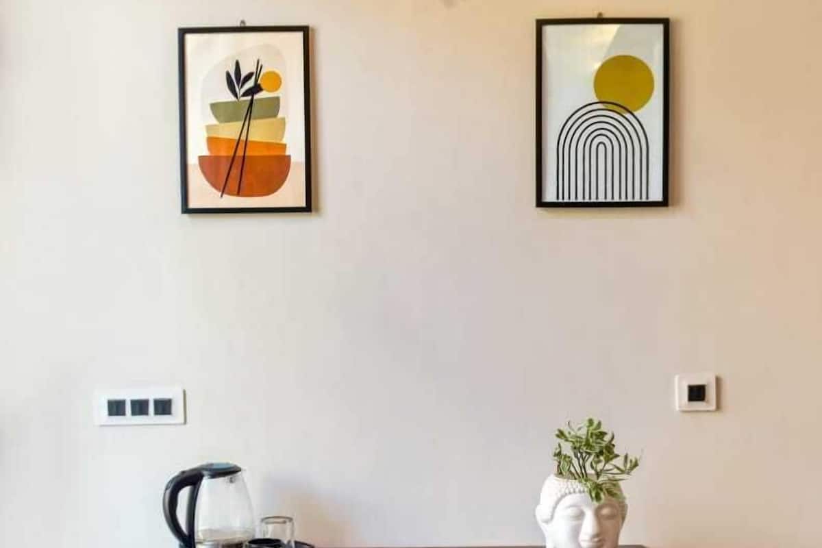 Uma secretária de madeira com uma cadeira, uma máquina de café e um vaso com uma planta. Duas obras de arte emolduradas estão na parede acima da secretária.