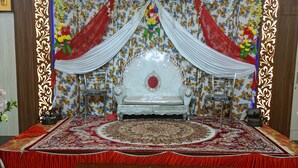 Um palco com um sofá branco e ornamentado, cortinas vermelhas e decorações florais.